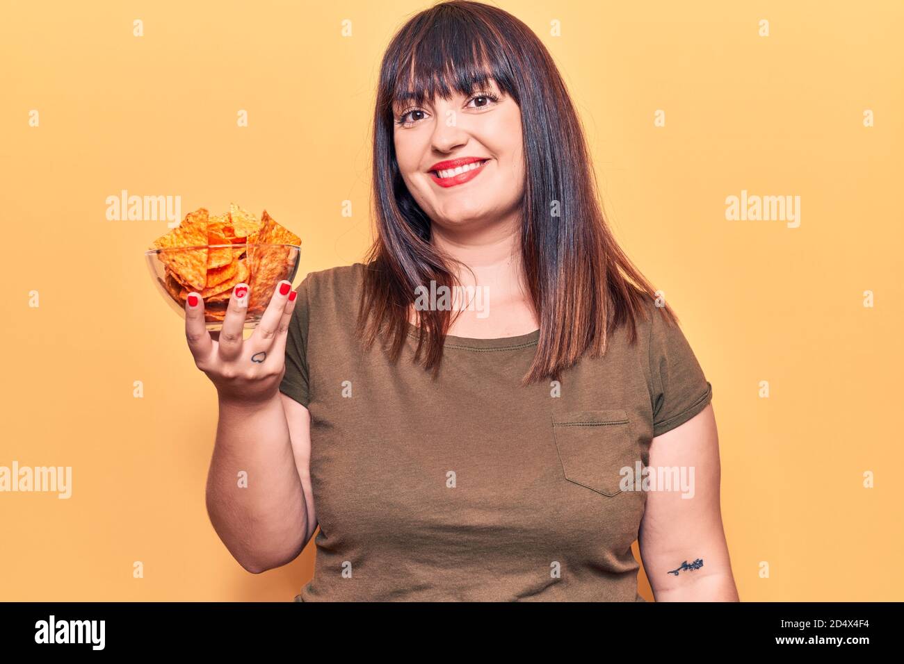 Young plus size woman holding nachos potato chips looking positive and ...