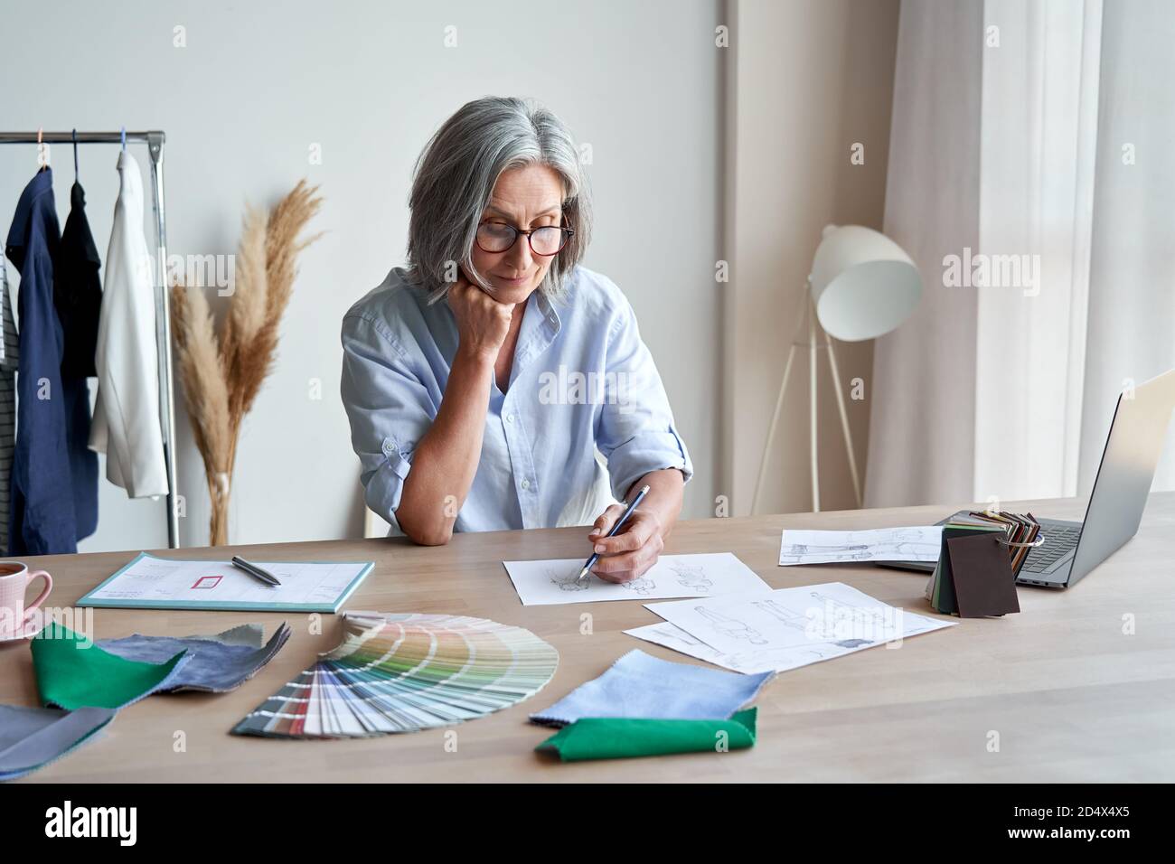 Senior elegant female fashion designer drawing sketches in studio ...