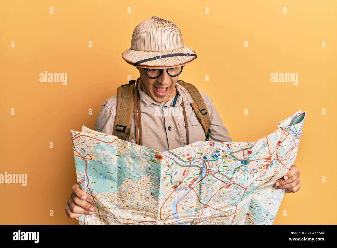 Middle age bald man wearing explorer hat holding map celebrating crazy ...