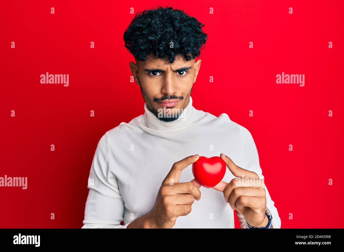 Young arab handsome man holding heart skeptic and nervous, frowning ...