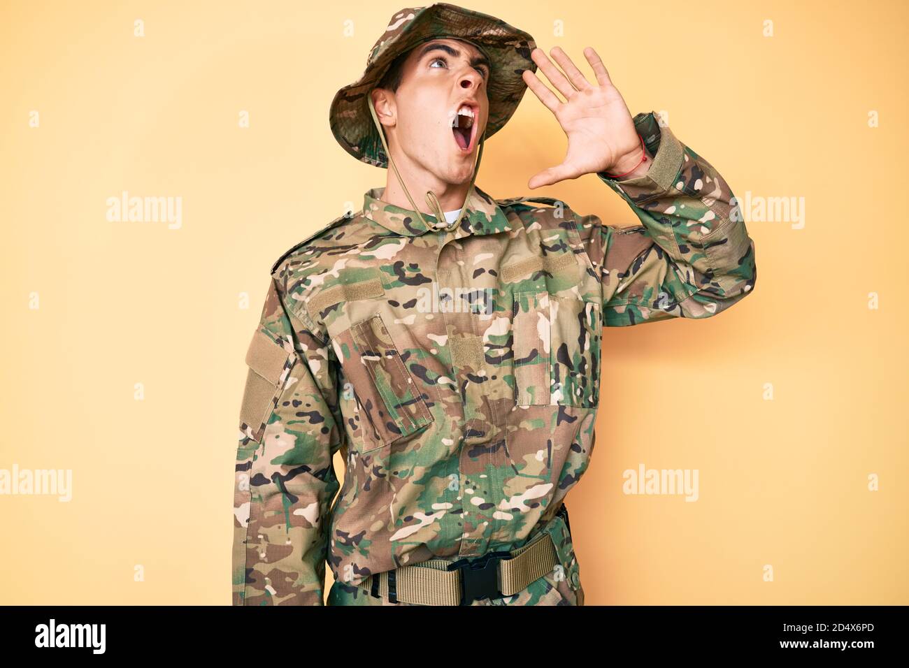Young handsome man wearing camouflage army uniform shouting and ...