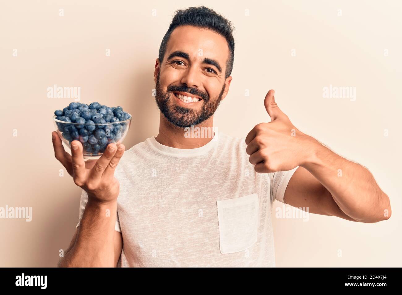 Young hispanic man holding blueberries smiling happy and positive ...