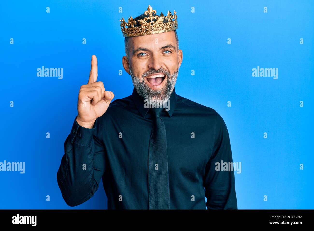 Middle age handsome business man wearing king crown pointing finger up ...