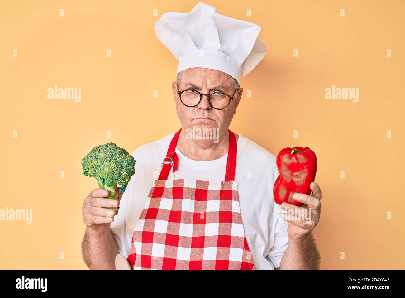 Senior grey-haired man wearing professional cook apron holding broccoli ...