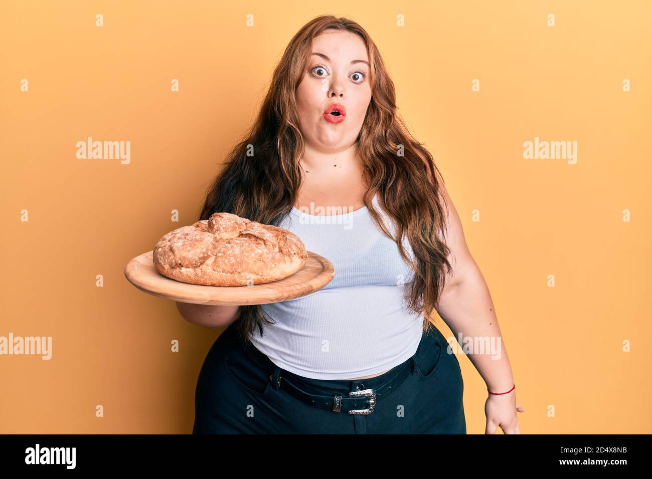 Plus size caucasian young woman holding bread scared and amazed with ...
