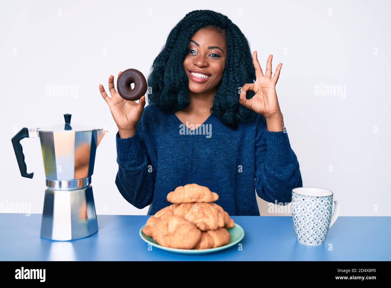Beautiful african woman eating breakfast holding cholate donut doing ok ...