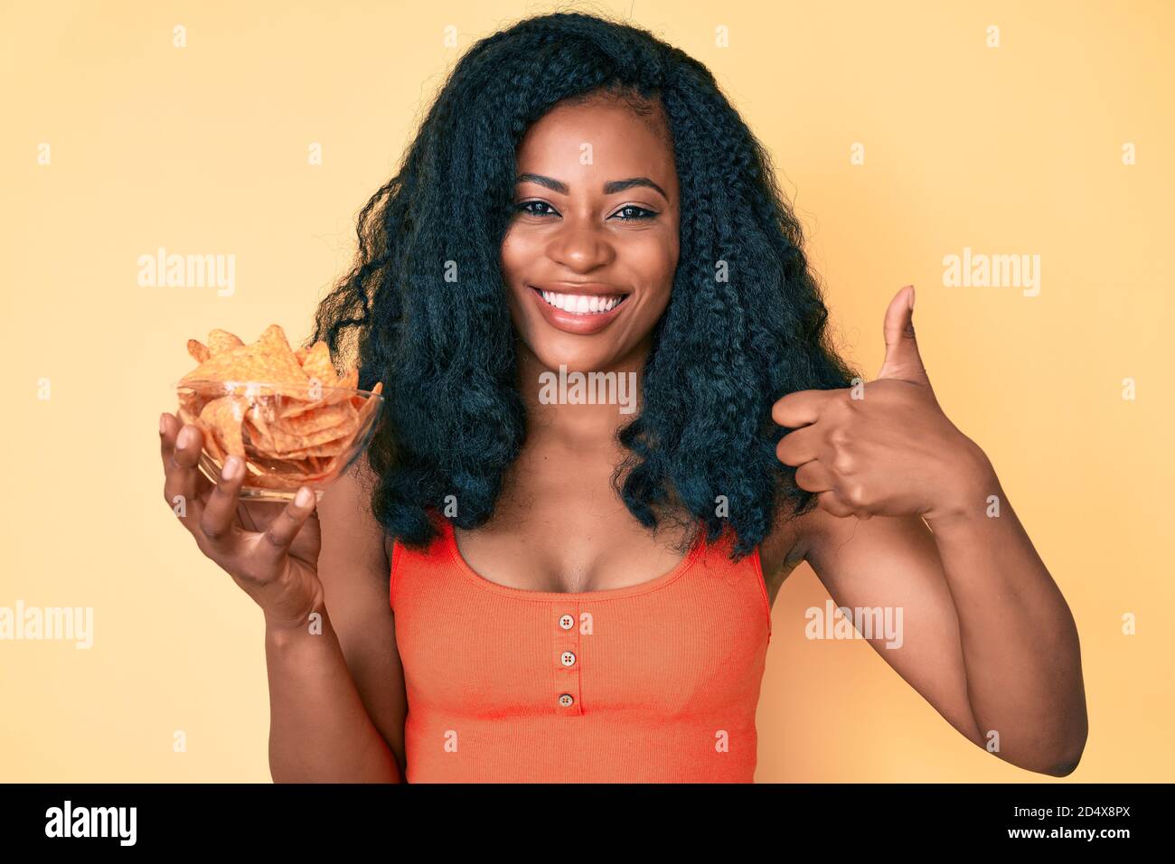 Beautiful african woman holding nachos potato chips smiling happy and ...