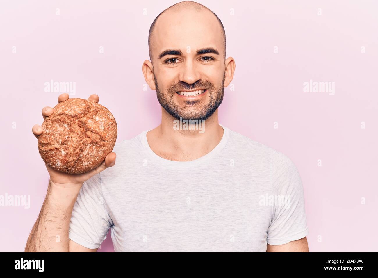 Young handsome bald man holding bread looking positive and happy ...