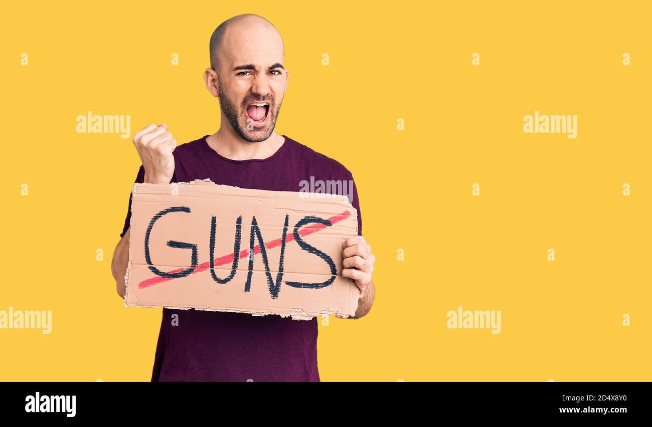 Young handsome man holding prohibited guns banner screaming proud ...