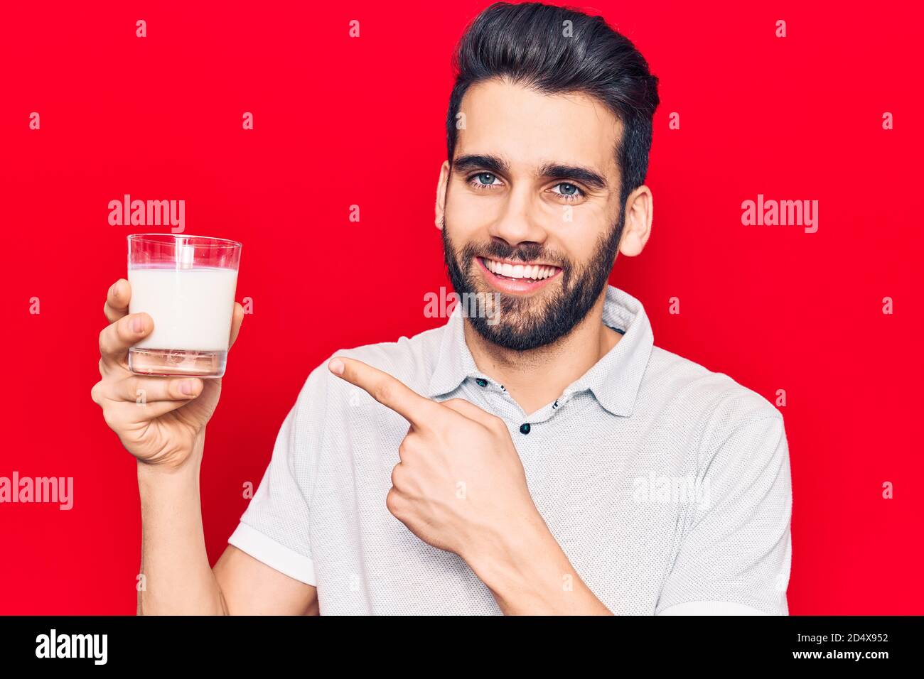 Young handsome man with beard drinking glass of milk smiling happy ...