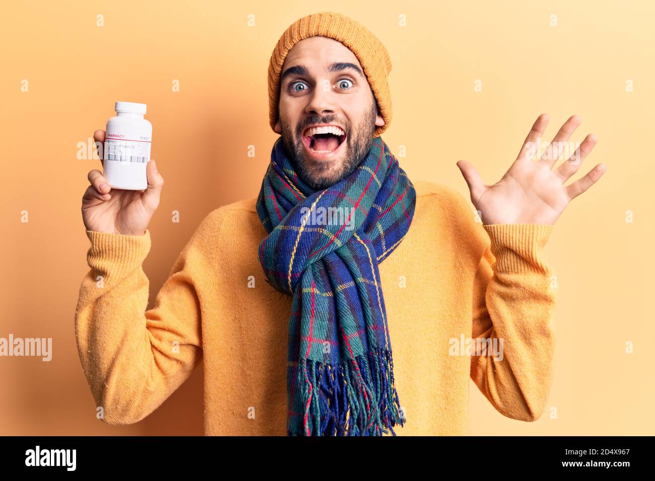 Young handsome man with beard holding bottle of pills celebrating ...