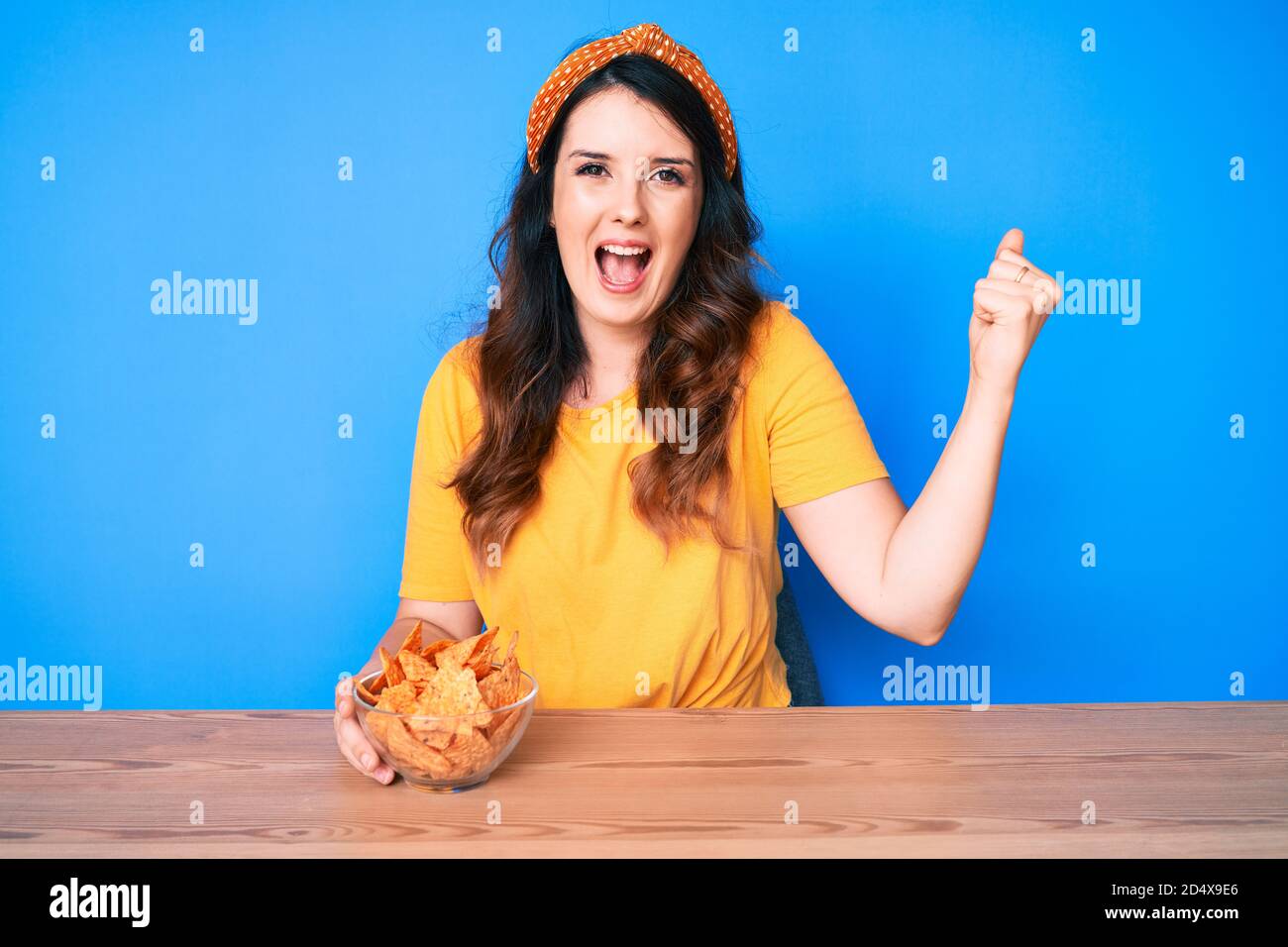 Young beautiful brunette woman sitting on the table eating nachos ...