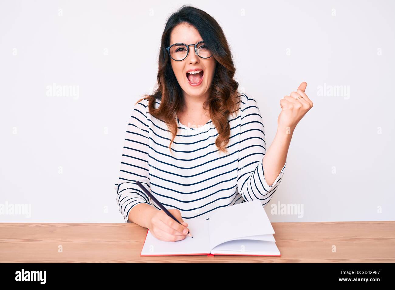 Young beautiful brunette woman writing book sitting on the table ...
