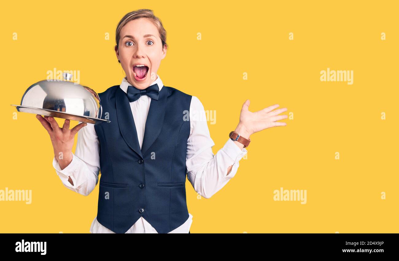 Young beautiful blonde woman wearing waitress uniform holding tray ...