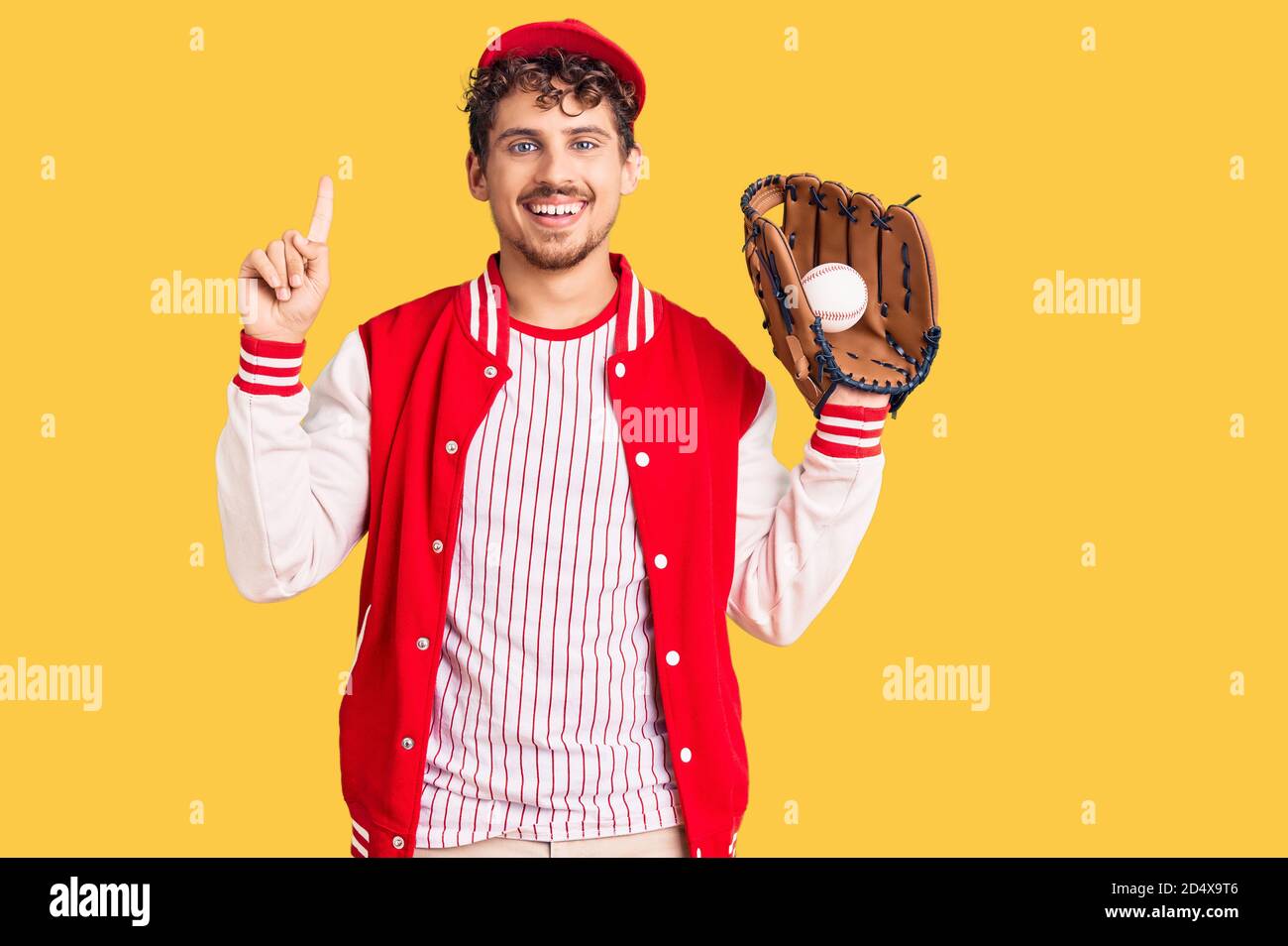Young handsome man with curly hair wearing baseball uniform holding ...