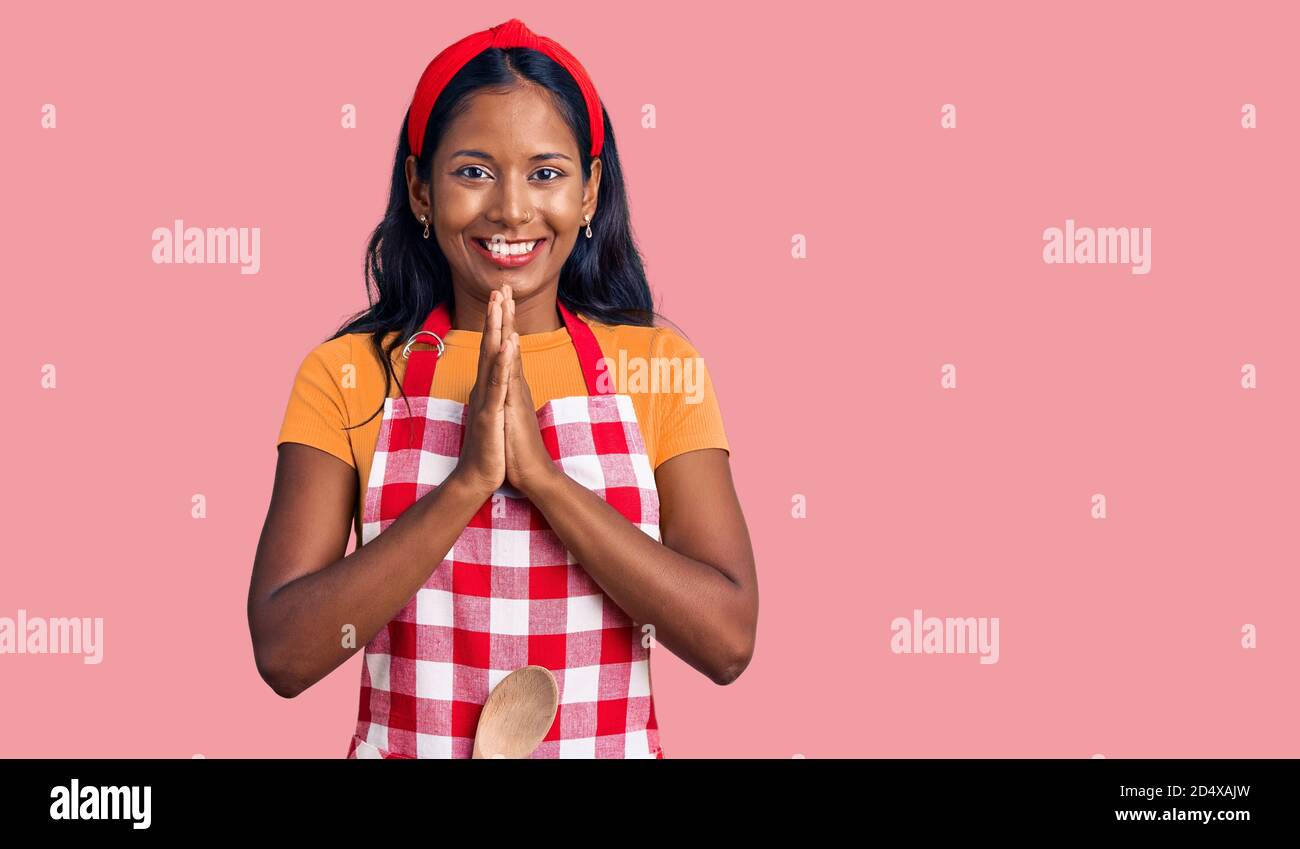 Young indian girl wearing professional baker apron praying with hands ...