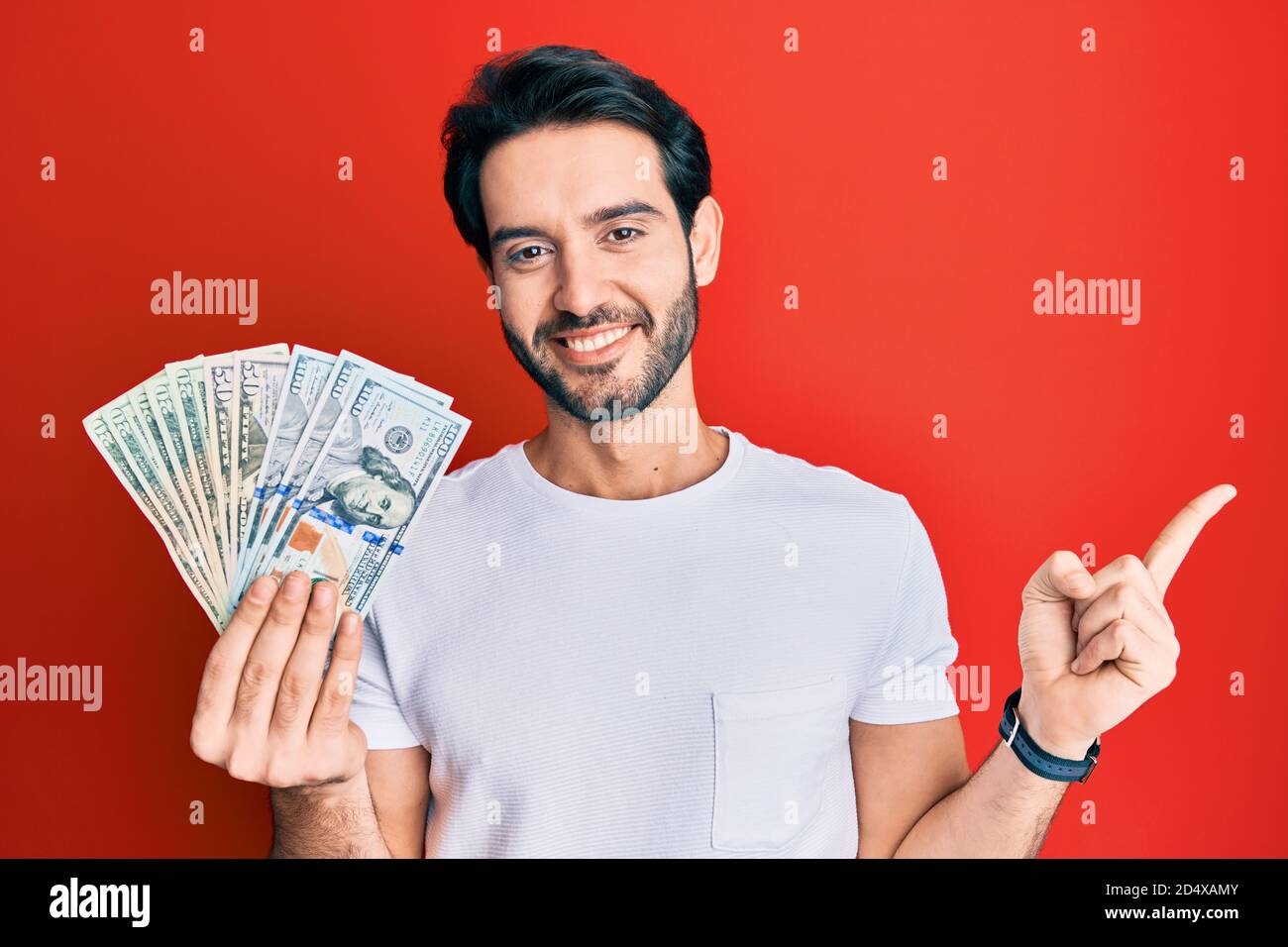 Young hispanic man holding dollars smiling happy pointing with hand and ...
