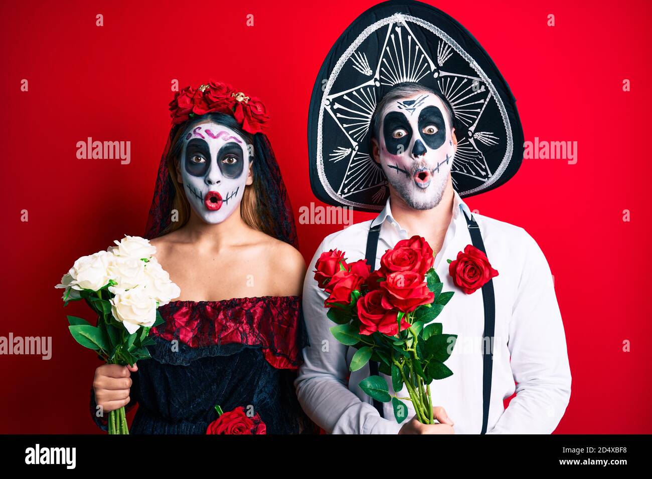 Couple wearing day of the dead costume holding flowers scared and ...