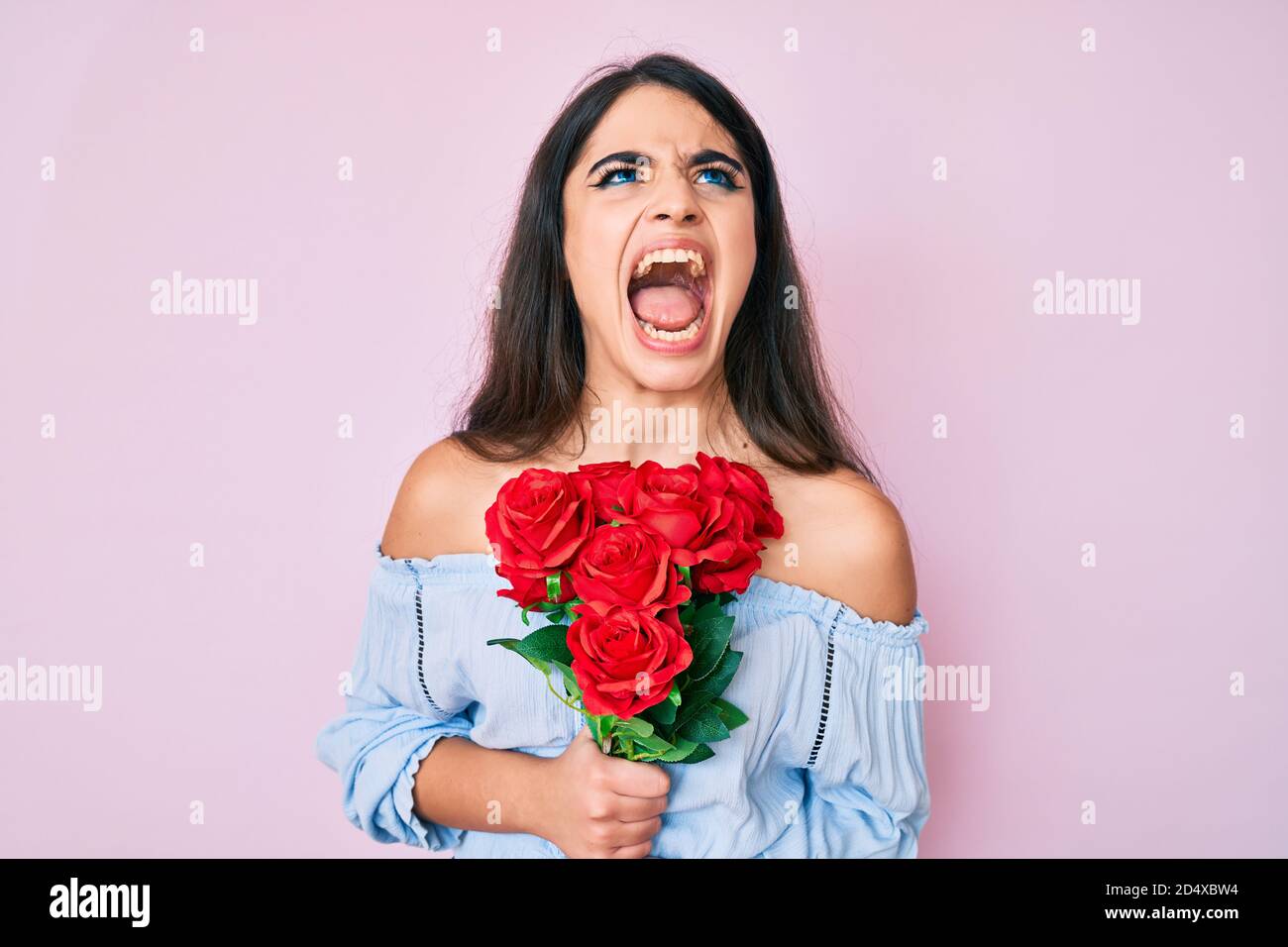 Brunette teenager girl holding flowers angry and mad screaming ...