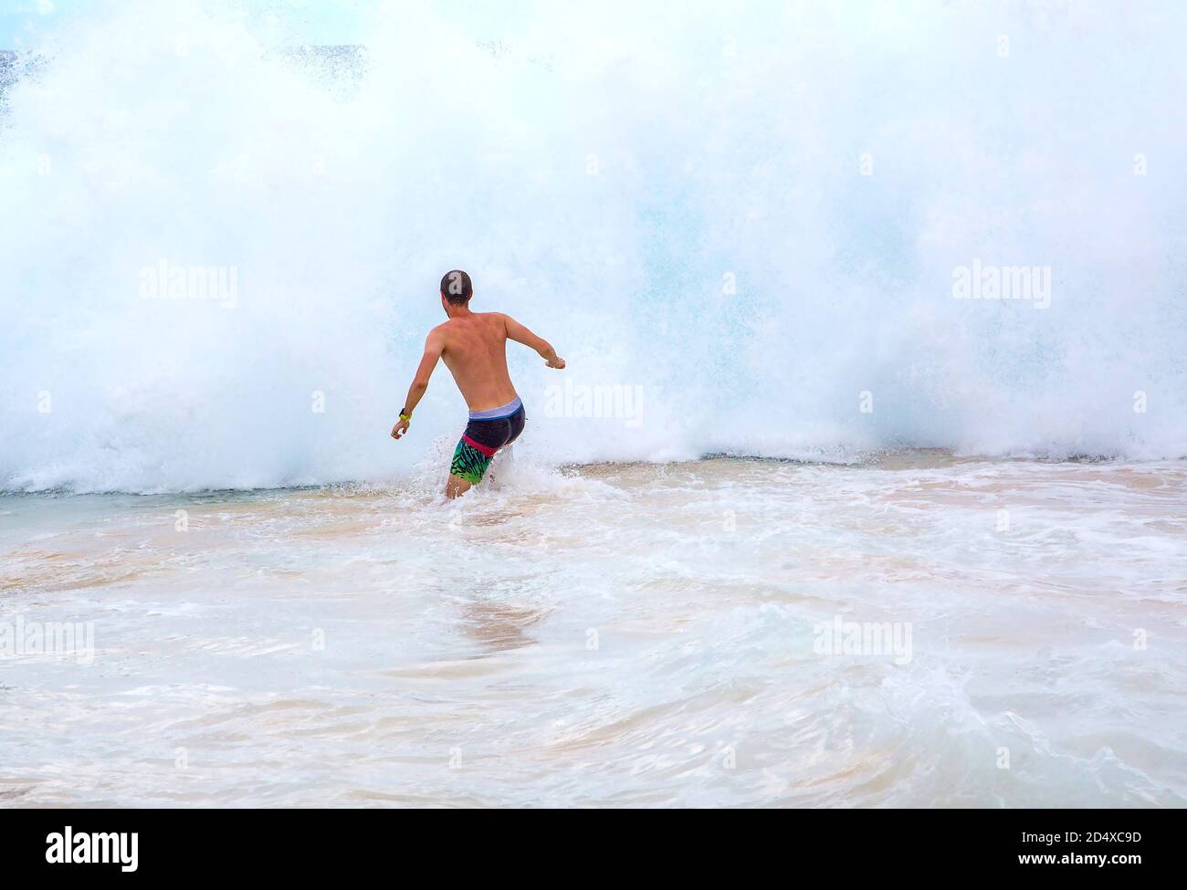 Caucasian young man running into the waves at the beach near Honolulu ...