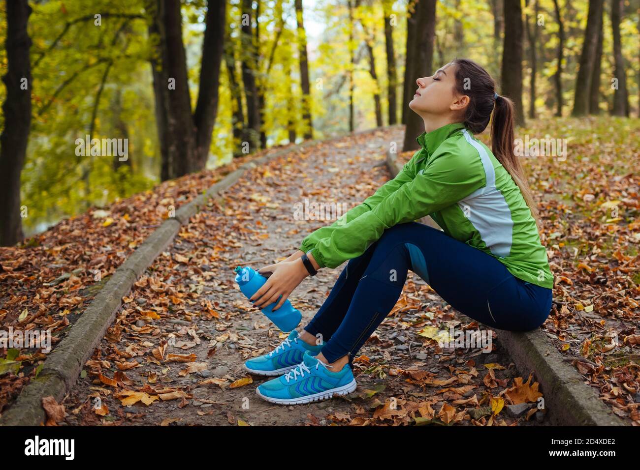 Runner having rest after workout in autumn park. Tired woman holding ...