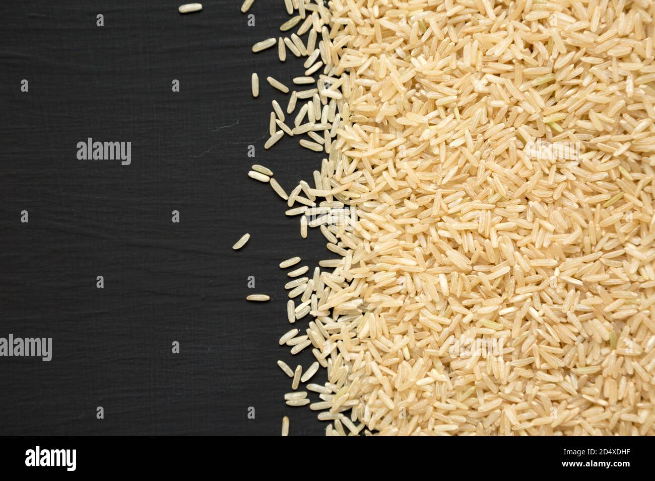 Dry Brown Rice on a black surface, top view. Overhead, from above, flat ...