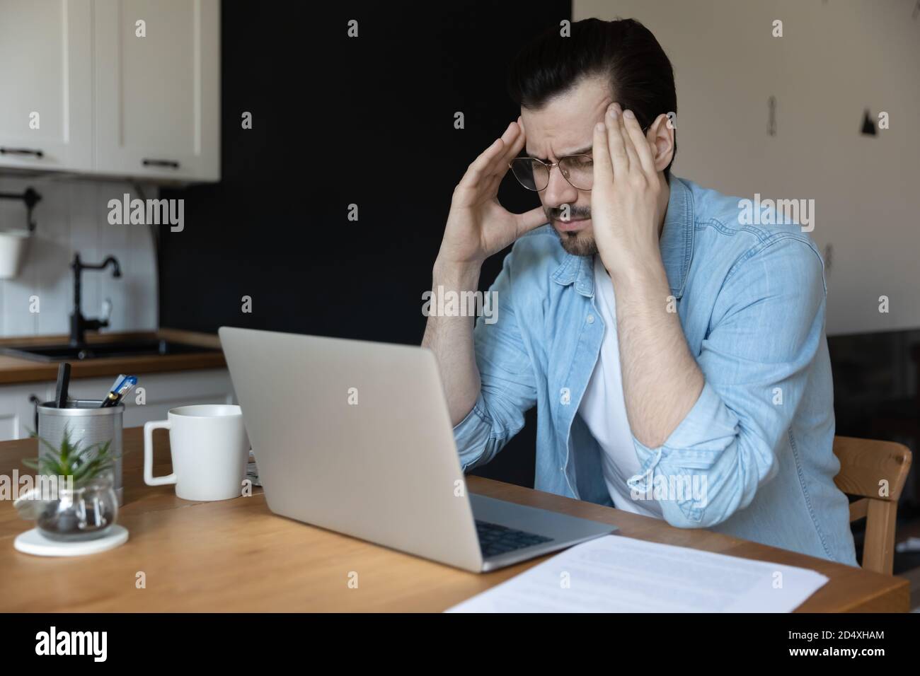 Overworked young man suffering from headache at home office Stock Photo ...