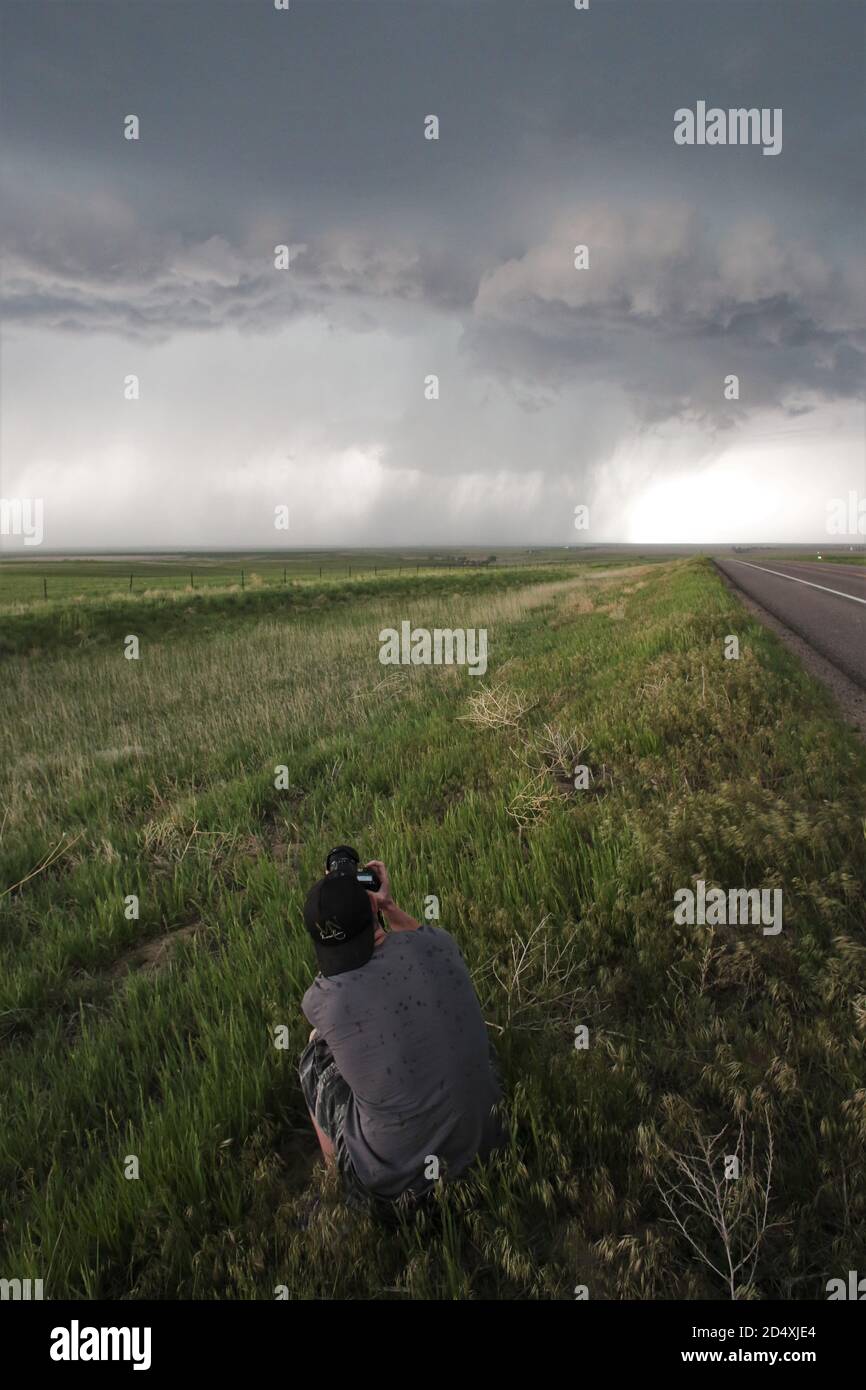 A man crouching on the ground and photographing a storm in the distance ...