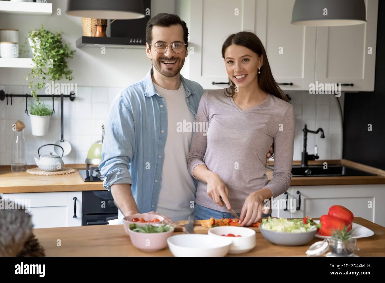 Portrait of happy young married couple cooking together in kitchen ...