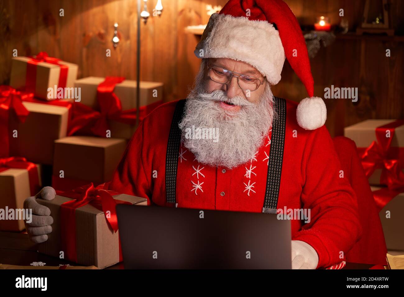 Happy Santa holding gift box using laptop sitting at table on Christmas ...
