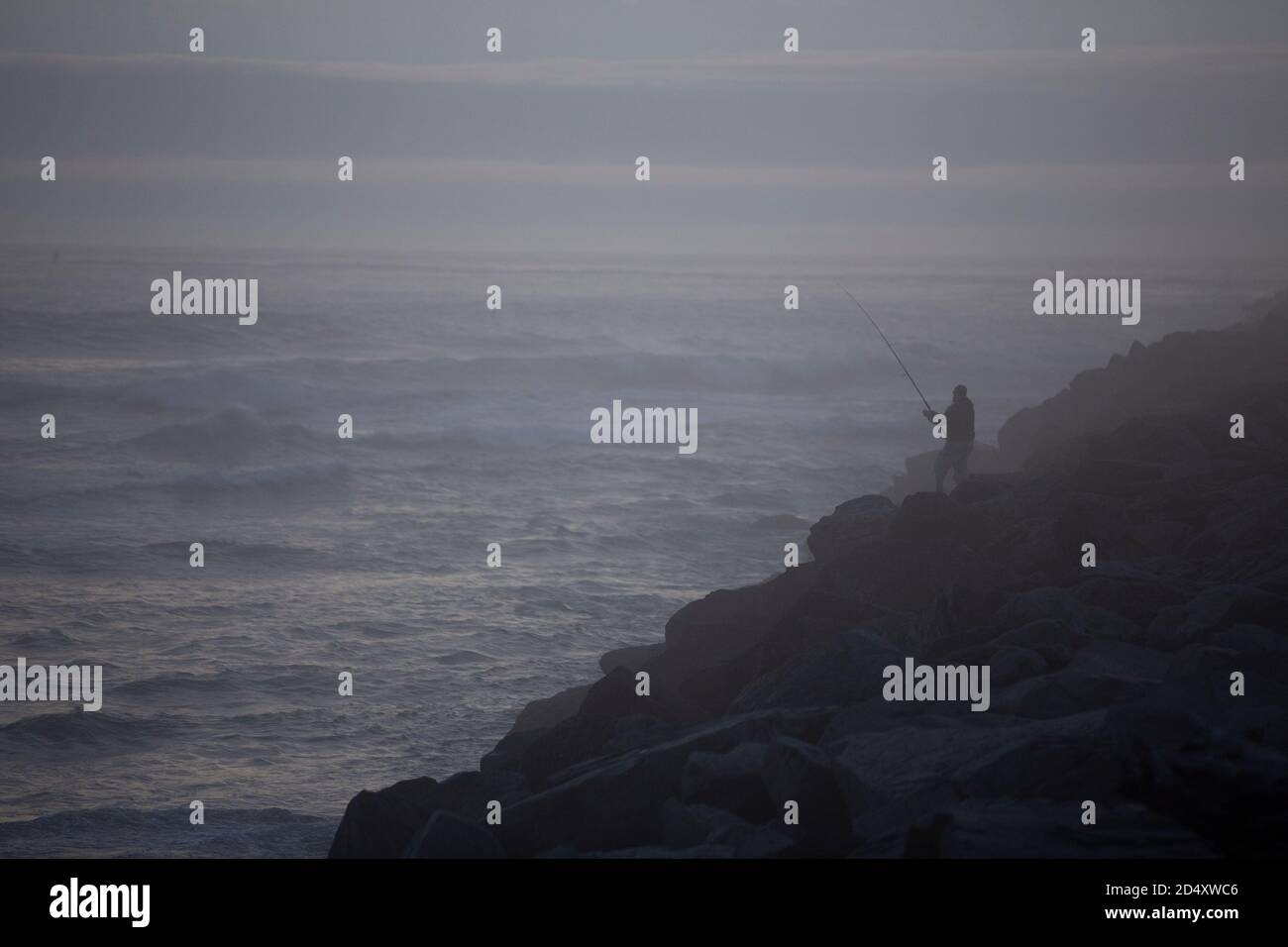 Outline of a fisherman on a foggy day sitting on a rocky outcropping ...