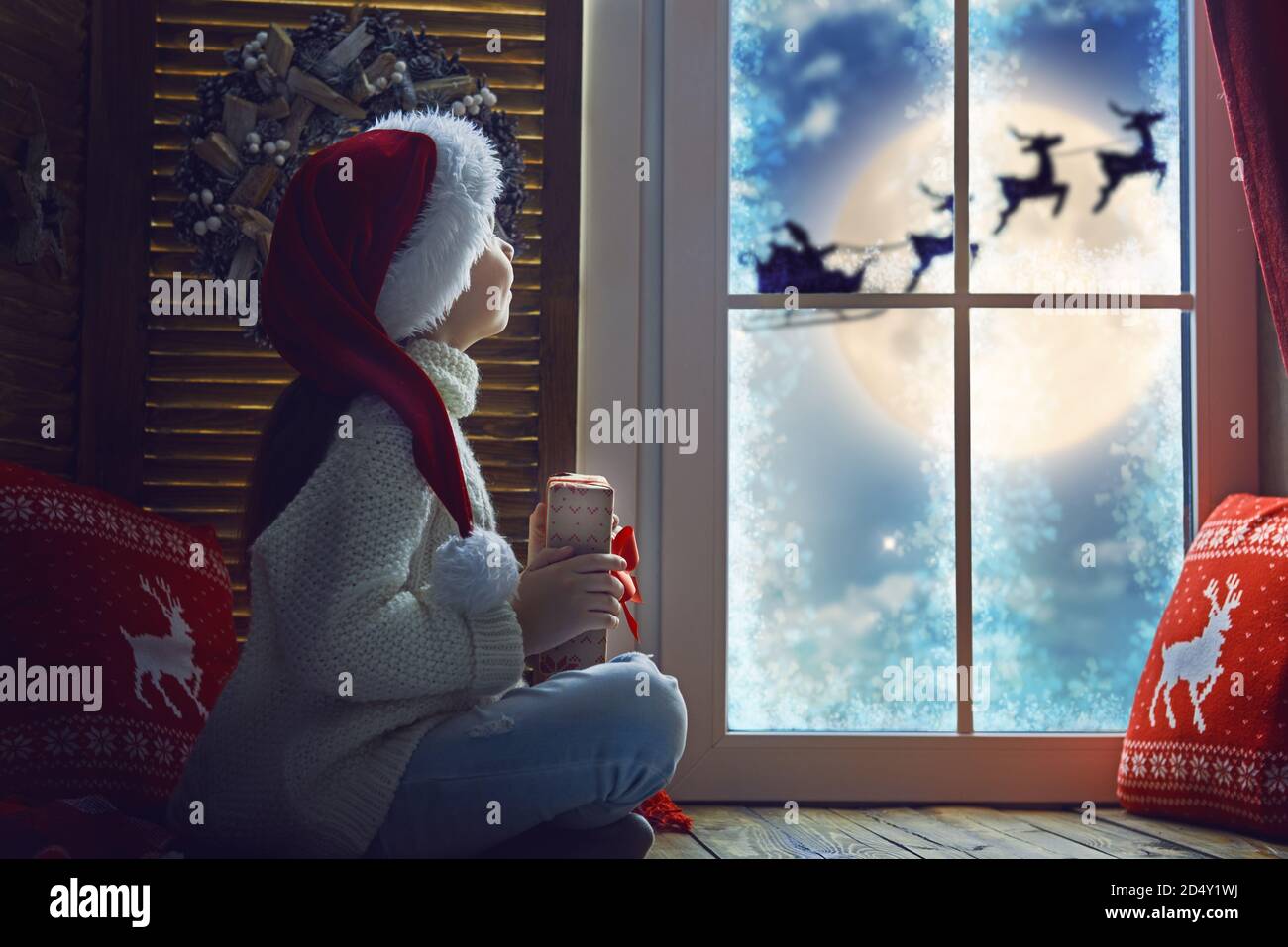 Cute little child girl sitting by window and looking at Santa Claus ...