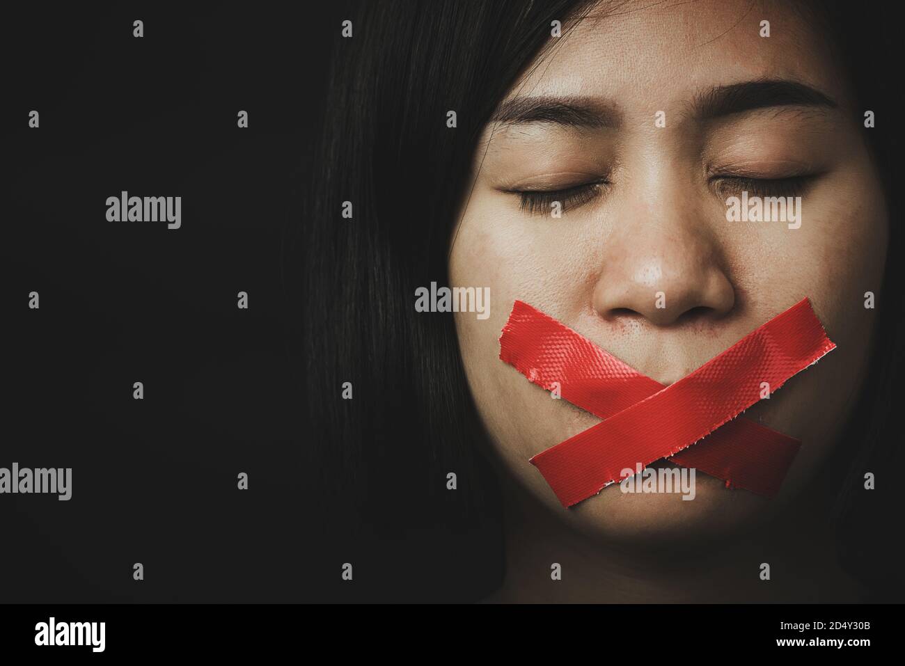 Asian woman blindfold wrapping mouth with red adhesive tape on black background. Freedom speech ...
