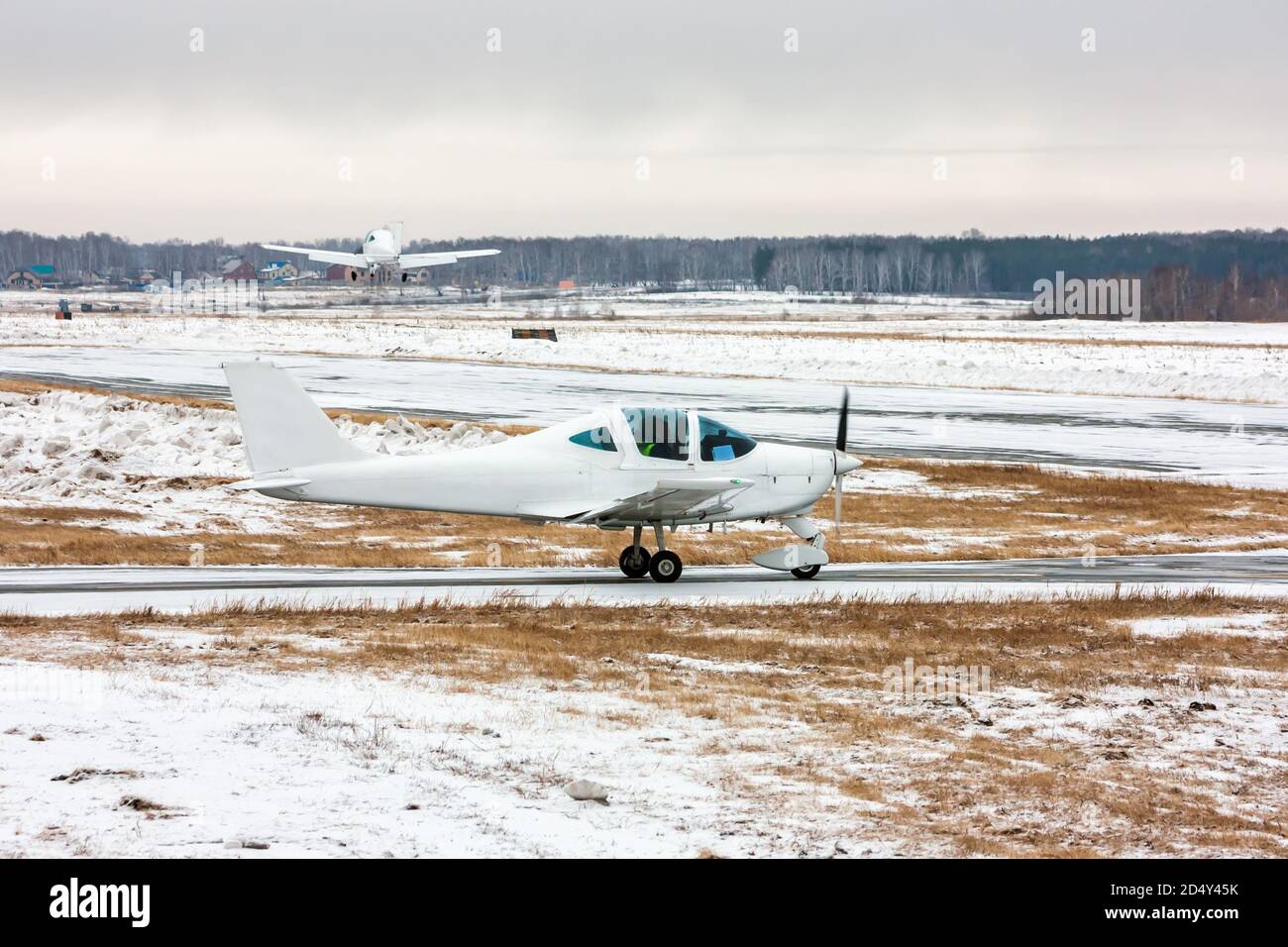 Small airplane moves on the taxiway and behind plane takes off at a cold winter airfield Stock ...