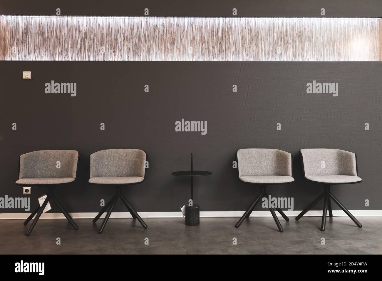 in front of a grey wall stand four equal chairs and a small table Stock ...