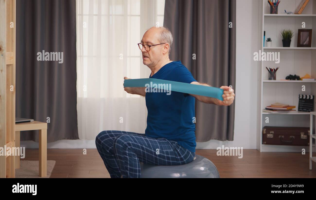 Strong senior man working out in living room using balance ball and ...