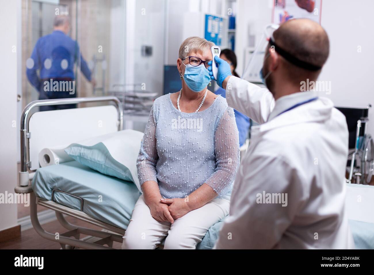 Medical staff using infrared thermometer to measure elderly woman ...
