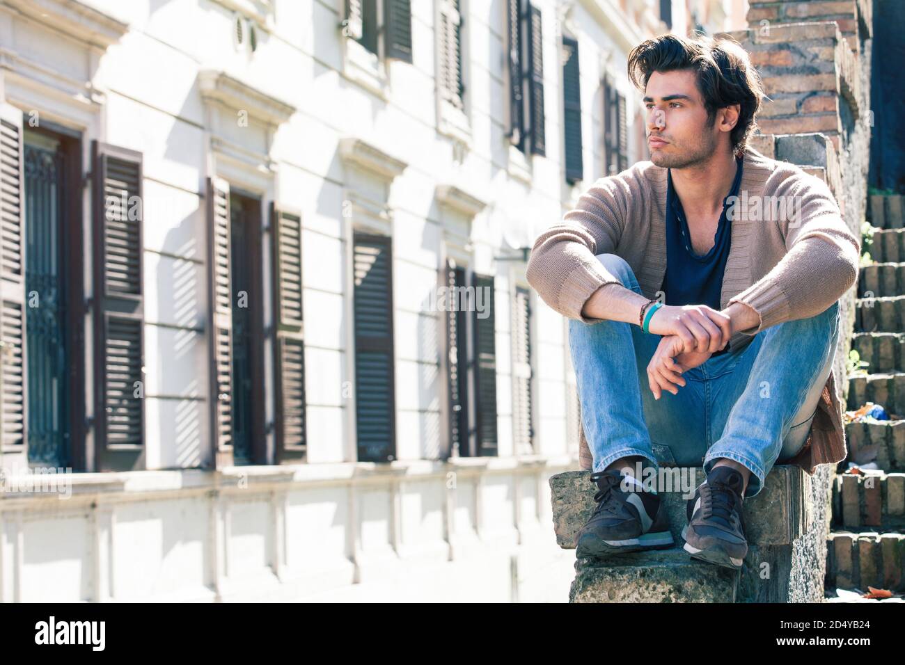 City young handsome man. Urban sitting model. Building windows. A ...