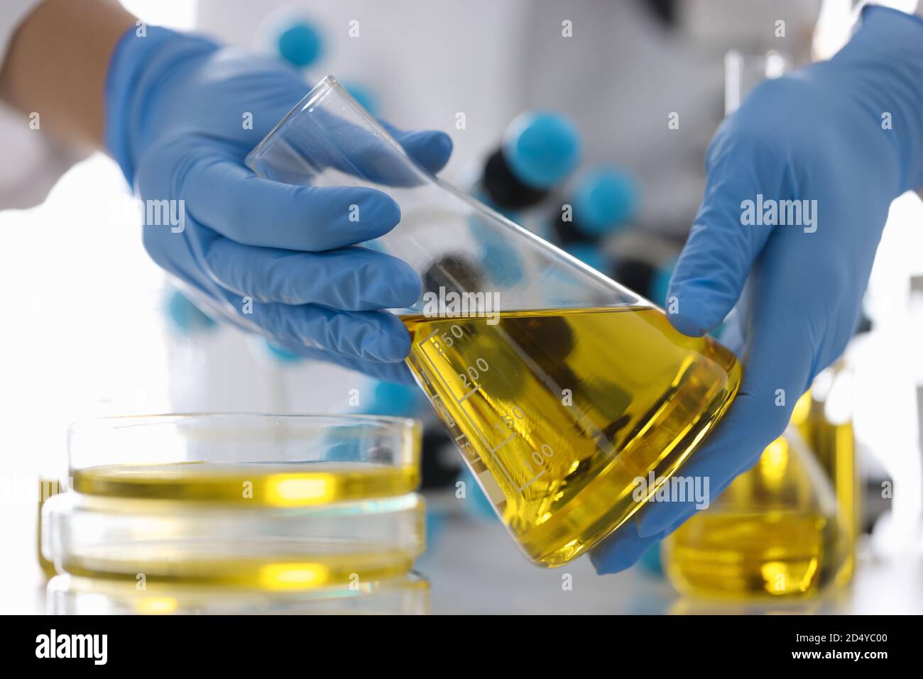 Hands in rubber gloves hold flask with yellow liquid in chemical ...