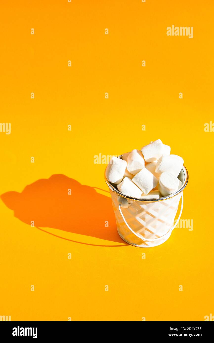 White marshmallows in a white metal bucket on a yellow background copy ...
