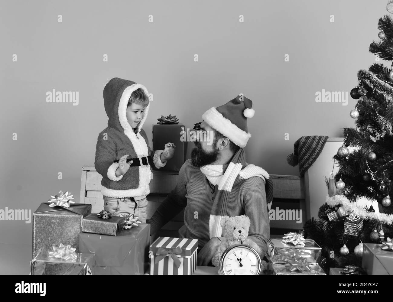 Santa and little assistant among gift boxes. Man with beard and curious ...