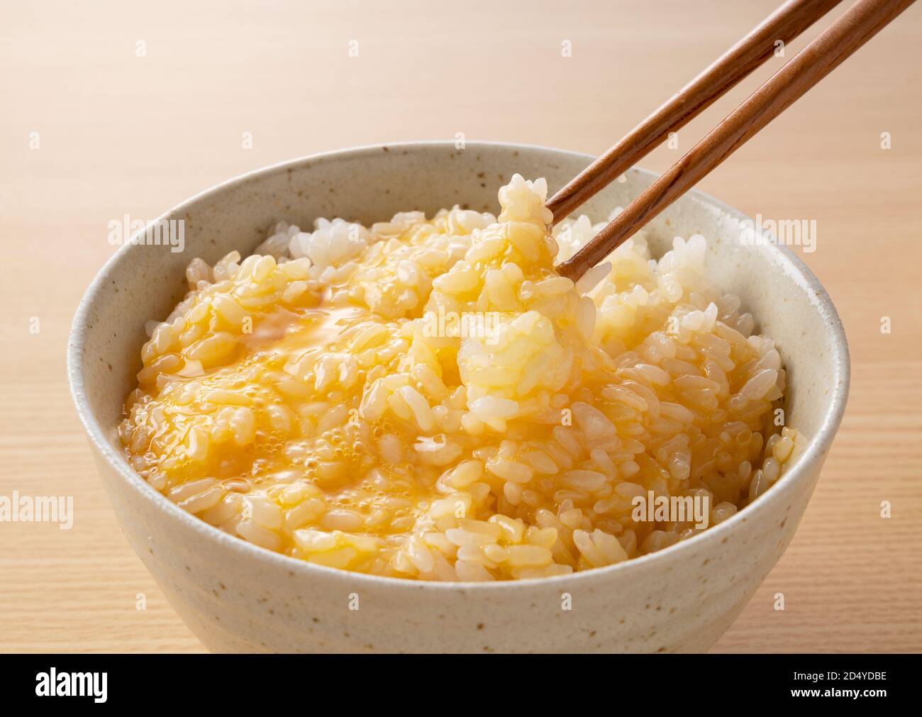 Scooping rice with chopsticks with a Japanese egg on the wooden ...