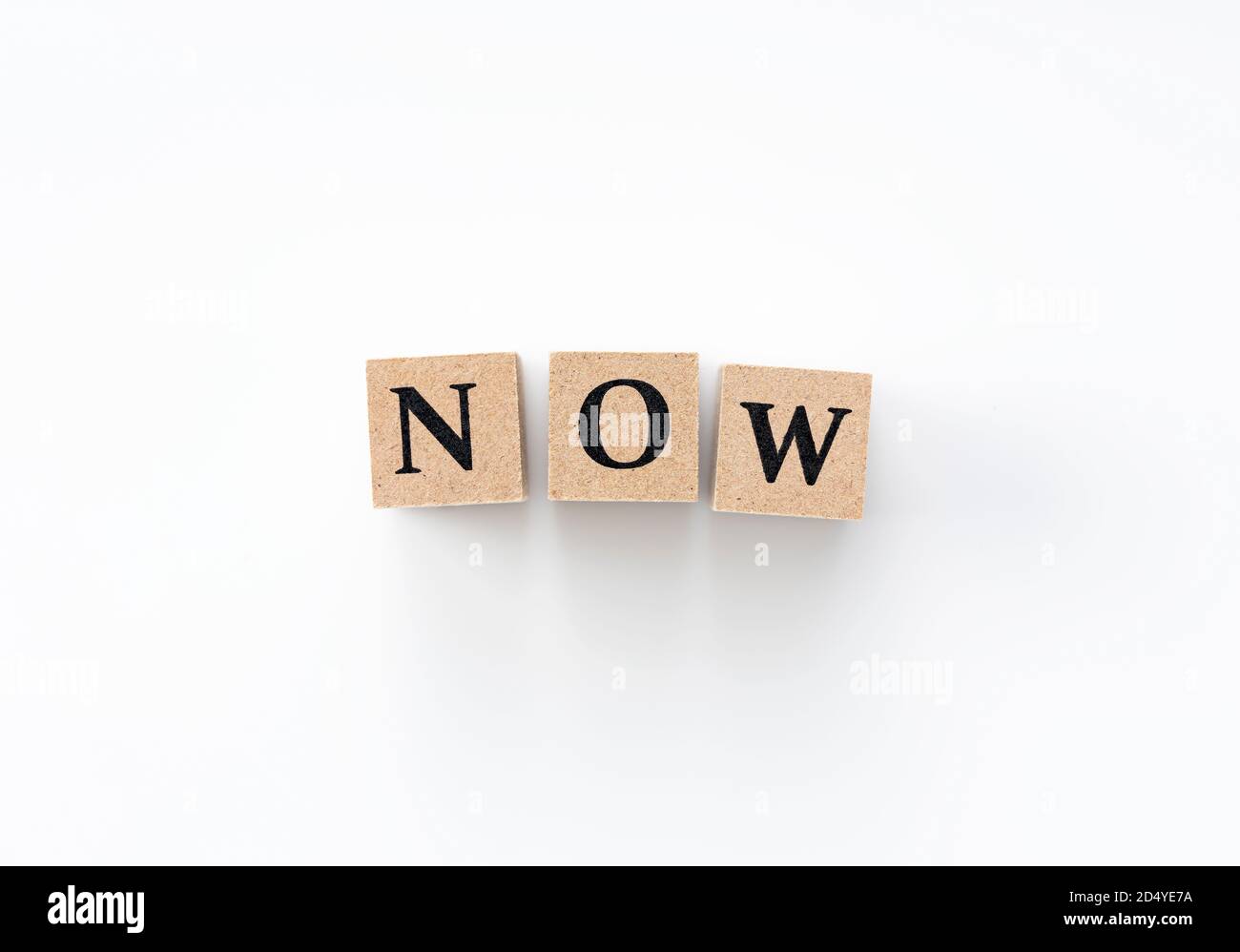 A wooden block with the word NOW written on it on a white background ...