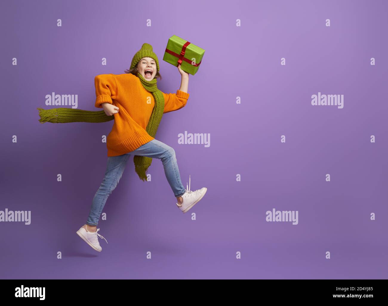 Happy little girl with Christmas gift on bright color background ...