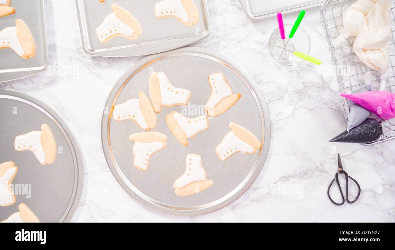 Flat lay. Decorating ice skate shaped sugar cookies with white color ...