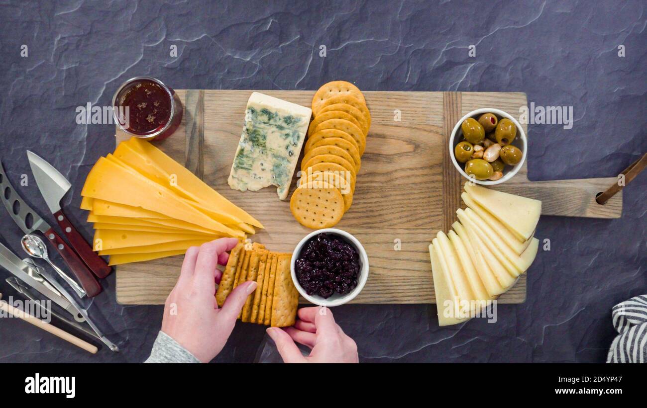 Flat lay. Arranging gourmet cheese, crakers, and fruits on a board for ...