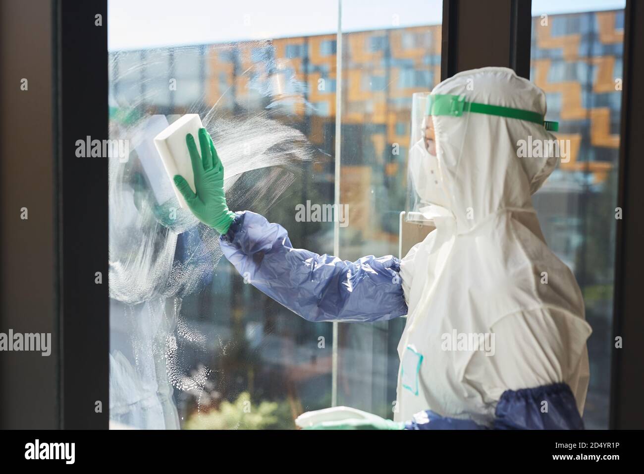 Side view portrait of female worker wearing hazmat suit washing windows ...
