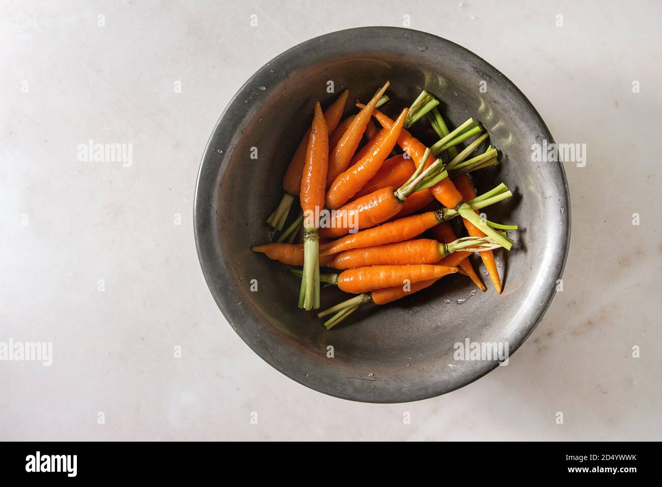 Young mini carrot in vintage metal bowl over white marble background ...