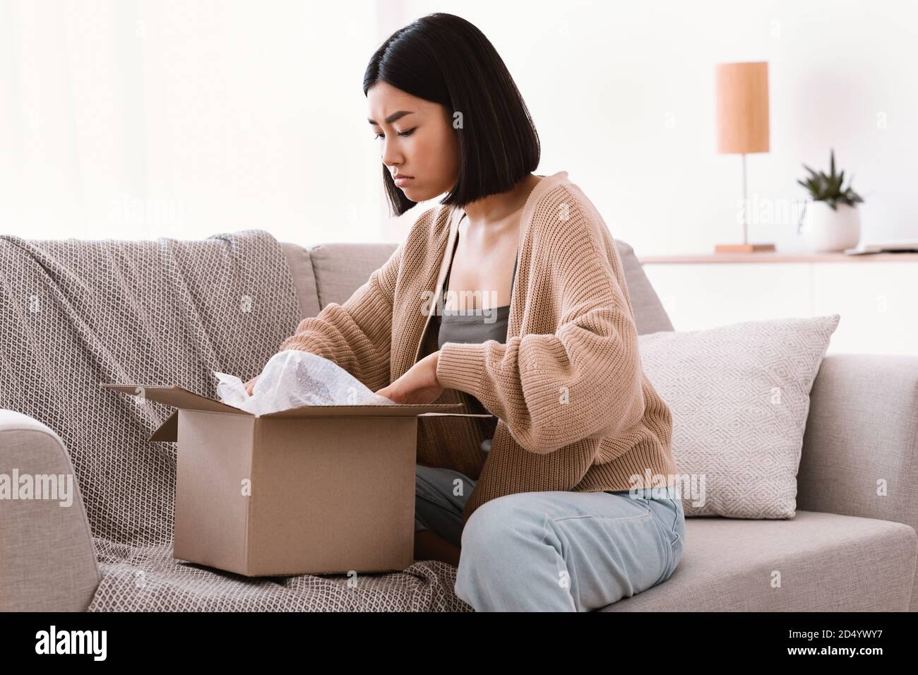 Confused young woman unpacking wrong parcel, delivery mistake Stock ...