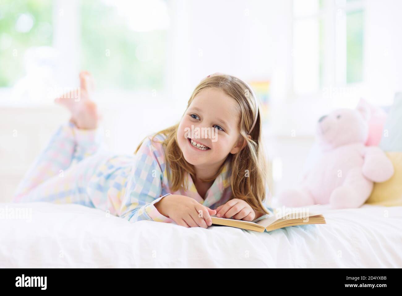 Child reading book in bed in white sunny bedroom with window. Children ...
